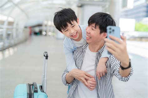 여행 가방을 든 아시아 어린 소년은 화창한 날에 공항 스카이 워크에서 아버지를 껴안고 어머니와 셀카를 찍습니다 휴가 중 여행