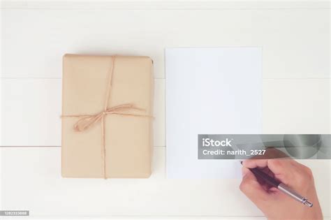 빈 인사말 카드와 편지를 쓰고 나무 테이블에 크래프트 종이와 선물 상자를 갖는 사람의 손 선물 및 패키지 엽서 모형 상단 보기 평면 누워 복사 공간 휴일 개념 12월에 대한