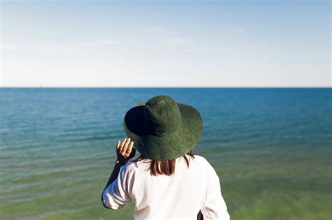 해변 절벽에 서 서 맑은 저녁에 바다를 바라보는 모자에 있는 세련 된 소녀 일몰에 해변에서 편안한 모자에 행복 한 젊은 보헤미안