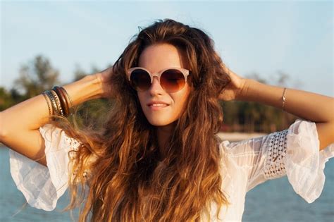 Feche o retrato de uma mulher linda em um vestido branco na praia tropical no pôr do sol usando