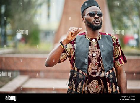 African Stylish And Handsome Man In Traditional Outfit And Black Cap Raised His Right Hand Up