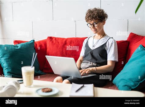 Young Busy Woman In Eyeglasses Typing On Laptop Keypad While Looking At