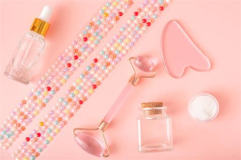핑크 석영 스톤 롤러 페이셜 구아 샤와 유리 화장품 병은 라인 스톤과 파스텔 핑크 배경에 있습니다 얼굴 트리트먼트 및 스파 천연