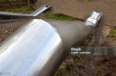 잔디 언덕과 나무 팔리세이드가있는 필드에 스테인레스 스틸 슬라이드 타탄 고무 패드에 영향을 미치는 어린이를 슬라이딩하기위한 대형 광택 튜브 튜브의 끝은 열린 쓰루입니다 0