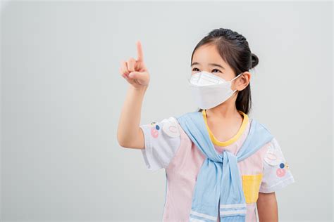 코로나바이러스 발생을 보호하기 위해 인공 호흡기 마스크를 쓰고 빈 배경에 손을 가리키는 아시아 어린 소녀 새로운 바이러스