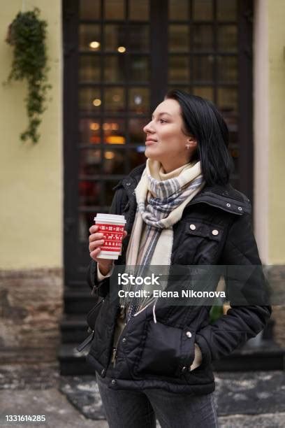 어깨 길이의 머리를 가진 아름다운 갈색 머리는 따뜻한 옷을 입고 거리에 서서 그녀의 손에 빨간 골판지 컵을 들고 옆으로 보인다 30 34세에 대한 스톡 사진 및 기타 이미지