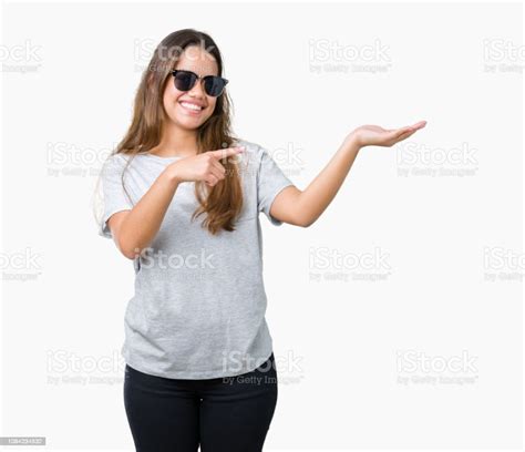 젊은 아름 다운 갈색 머리 여자 놀라게 했 고 손으로 제시 하 고 손가락으로 가리키는 동안 카메라에 웃 고 고립 된 배경 위에