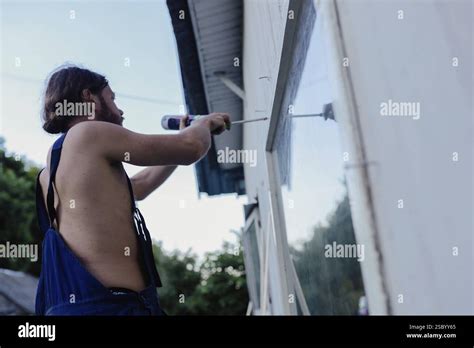 A Man Applying Sealant To A Window Frame Of A Wooden Structure During