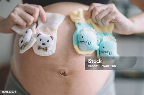 쌍둥이 아기 출산을 기대하는 그녀의 배 앞에서 2 쌍의 아기 부츠를 들고있는 아시아 중국 임신 한 아가씨에 클로즈업 쌍둥이에
