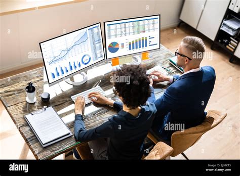 Side View Of Male And Female Stock Market Broker Analyzing Graphs On Laptop At Workplace Stock