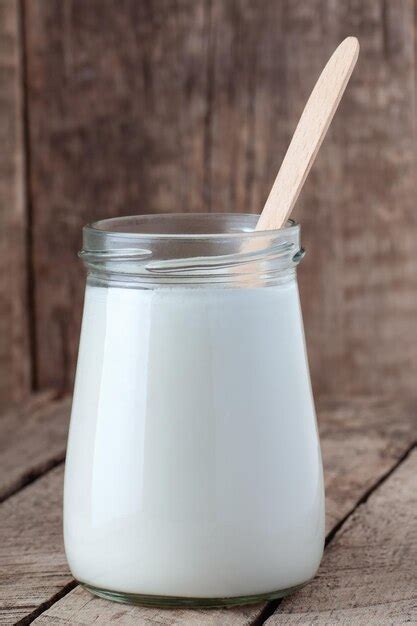 Premium Photo Greek Yogurt In A Glass Jar With Spoon On Wooden Background