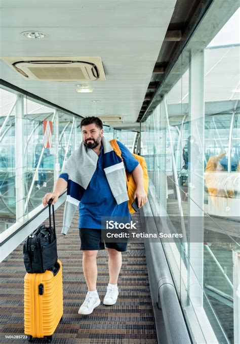 노란색 여행 가방과 배낭 탑승 비행기를 가진 남자가 현대 공항의 유리 탑승 복도를 걷고 있습니다 여행 및 관광 비행기로 여행하는 수하물을 소지한 승객 45 49세에 대한