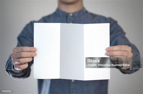 한 남자가 흰 종이를 들고 있다 남자의 손에 전단지 텍스트를 준비했습니다 회색 배경에서 격리 25 29세에 대한 스톡 사진 및