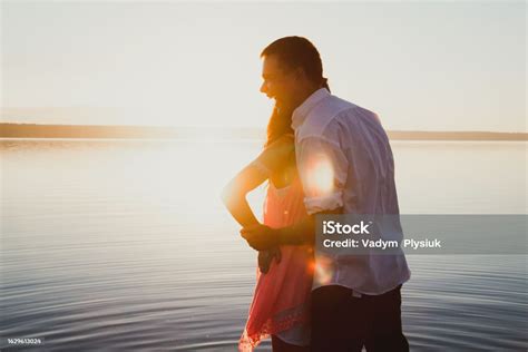 젊은 부부는 여름 해변에서 물속에서 웃고 있다 바다 위의 일몰 태양을 배경으로 한 두 개의 실루엣 갓 결혼한 부부가 껴안고 있다 낭만적 인 사랑 이야기 휴일 신혼 여행에서