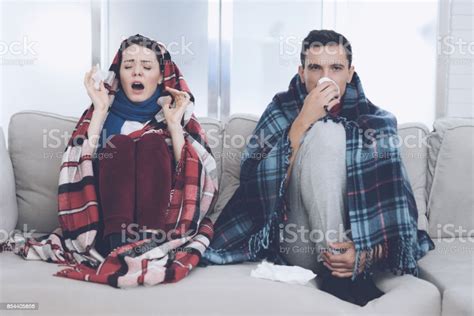 부부는 담요에 싸여 소파에 앉아 있다 남자와 여 자가 아 프 있습니다 남자는 밖으로 난다 재채기 하는 여자 감기와 독감에 대한