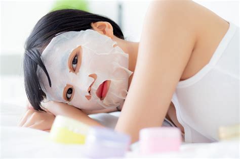 침실에서 침대에 시트 페이셜 마스크를 가진 아름다운 젊은 아시아 여성 미용 소녀는 집에서 주름 한 사람 스킨 케어 치료 및