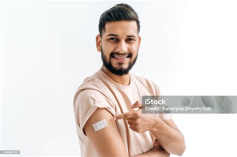 예방 접종 개념 젊은 인도 또는 아라비안 남자는 코로나 바이러스 및 기타 바이러스를 백신 보호받고 예방 접종 후 석고로 팔을 보여주고 고립 된 흰색 배경에 서서 미소