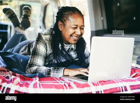 Senior African Woman Having Fun Inside Camper Van Using Laptop Computer