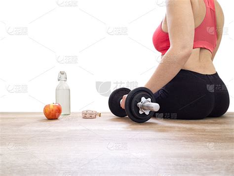 在白色背景下，一个不认识的女人拿着重量，卷尺，一个苹果和一瓶水