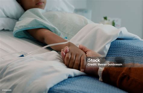 수술 후 병원에서 사랑과 지원 보살핌으로 침대에 누워 있는 아이와 손을 잡고 있습니다 어린이 의료 및 암 환자에게 공감 친절 연민을 가진 간병인과 도움 병원에 대한 스톡