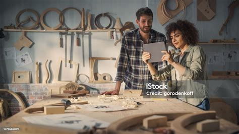 태블릿 컴퓨터를 사용하고 가구 워크샵에서 새로운 나무 의자 디자인을 논의하는 재능있는 두 명의 중소 기업 소유자 목수와 로프트
