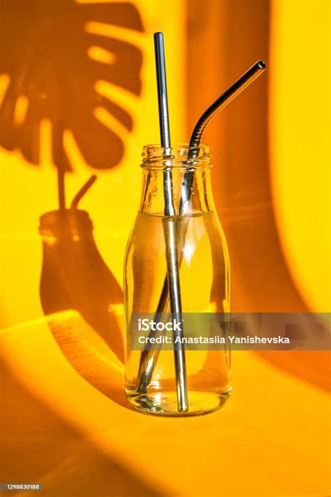 식물 그림자와 노란색 배경에 물이 유리 병에 재사용 가능한 금속 빨대 스테인레스 스틸 환경 친화적 인 마시는 짚 세트 폐기물이 없습니다 플라스틱 프리 물에 대한 스톡 사진