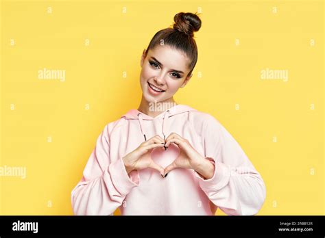 Young Smiling Pretty Woman Making Heart Symbol By Hands On Yellow