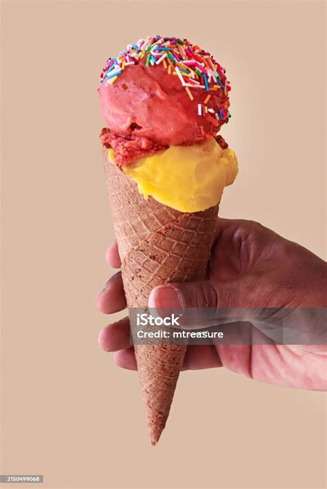 와플 콘을 들고 있는 알아볼 수 없는 사람 망고와 딸기 젤라토 아이스크림 두 스쿱 여러 가지 빛깔의 설탕 스프링클 베이지색 배경