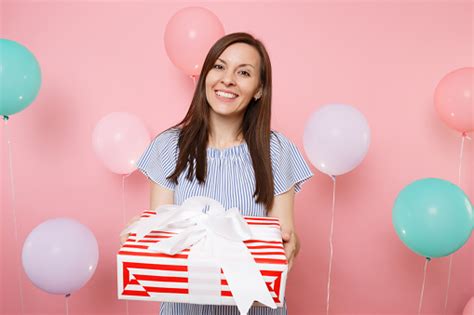 블루 드레스 선물 다채로운 공기 풍선 파스텔 핑크 배경에 빨간색 상자를 들고 웃는 매력적인 젊은 여자의 초상화 생일 휴가 파티