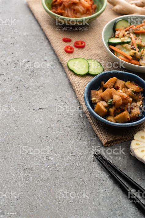 생강 근처 김치 얇게 썬 오이 칠리 페퍼를 콘크리트 표면에 젓가락 근처의 자루에 얹은 그릇의 선택적 초점 0명에 대한 스톡 사진