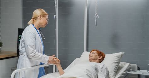 의사는 심각한 수술 후 침대에 누워있는 동안 손을 잡고 노인 여성과 이야기합니다 사진 Unsplash의 의사 이미지