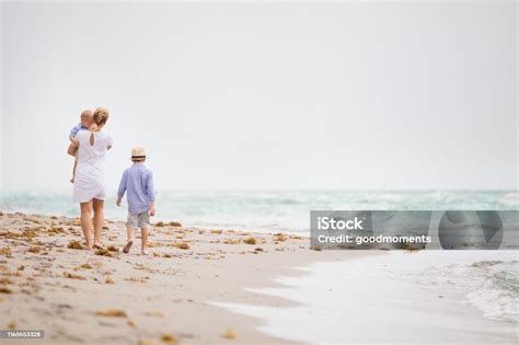 바다 해변을 따라 걷는 그녀의 두 어린 소년과 흰색 드레스를 입은 젊은 어머니 바다에서 휴가를 즐기는 아기와 소년과 여자 빈 해변에서 어머니 가족에 대한 스톡 사진 및 기타