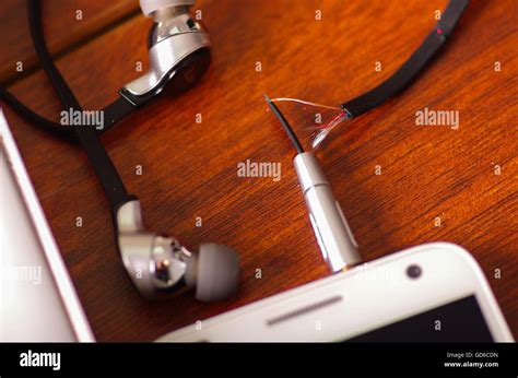 Broken Audio Headphones Cable Connected Into Smartphone Lying On Wooden Surface Part Of Wire