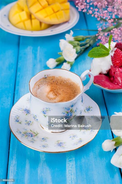 파란 꽃 및 과일 아이스크림 아름 다운 도자기 컵에 향기로운 커피 꽃과 푸른 나무 배경에 망고 아침 식사는 달콤한 거품 내기에