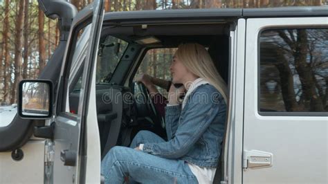 Young Blonde Woman Sits On The Passenger Seat In The Car Jeep And Talks