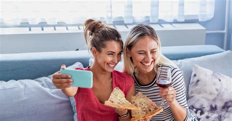 피자를 먹고 셀카를 위해 웃는 친구들 그들은 피자를 공유하고 모바일 스마트 폰에서 셀카 사진을 만들고 있습니다 그들은 집에서 파티를하고 피자를 먹고 재미있게 놀고