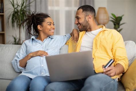 Happy African Couple Using Laptop Browsing Internet Sitting At Home