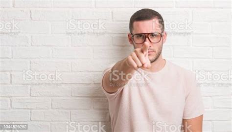 젊은 백인 남자 흰색 벽돌 위에 서 벽 카메라 하 고 당신에 게 손가락으로 가리키는 안경을 착용 손 기호 정면에서 긍정적이 고