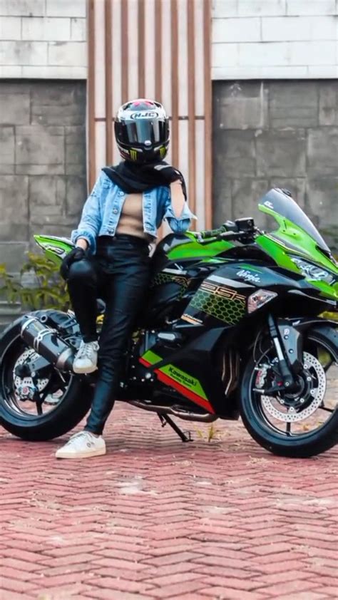 A Person Sitting On Top Of A Green And Black Motorbike In Front Of A Building