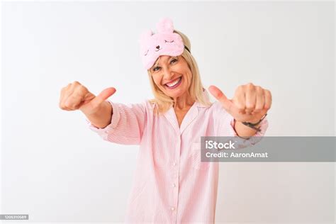 중년 여성은 손으로 긍정적 인 제스처를하고 승인 고립 된 흰색 배경 위에 수면 마스크와 잠옷을 입고 엄지 손가락으로 미소와