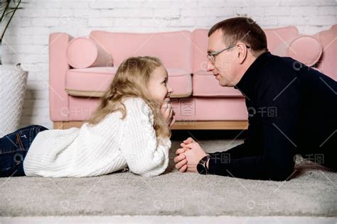 爸爸高清图片 父爱女儿拥抱爸爸躺在家里舒适明亮的房间里躺在粉红色沙发旁边的地板上黑白相间的衣服亲情观念与世代对立 父爱女儿拥抱爸爸躺在家里舒适明亮的房间里躺在粉红色沙发旁边的地板上黑白相间的