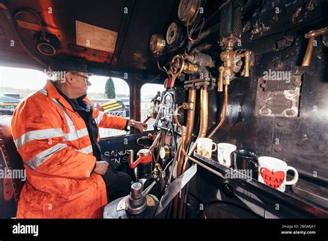 A Man Looks Out Of The Cab Whilst Driving The Locomtive Holding A