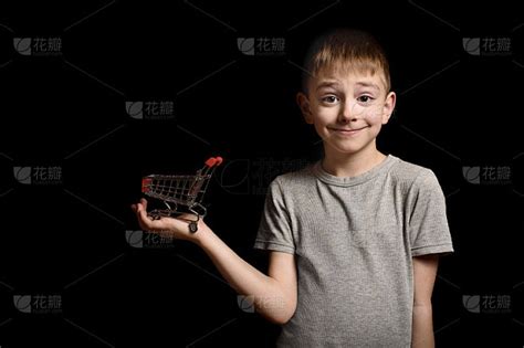 可爱的小男孩手里拿着一个金属购物手推车孤立在黑色背景上购物的概念副本的空间