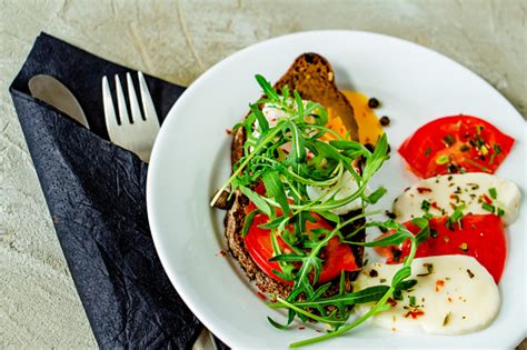 토마토 모짜렐라 아루굴라 향신료 후추 를 콘크리트 배경에 흰 접시에 얹은 검은 호밀 빵 조각에 맛있는 데친 달걀 0명에 대한