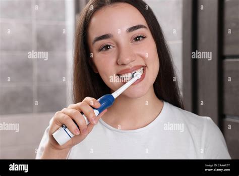 Young Woman Brushing Her Teeth With Electric Toothbrush In Bathroom
