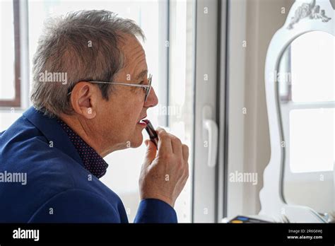 An Old Man Puts On Makeup And Looks In The Mirror A Senior Paints His