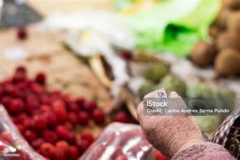 50 000 콜롬비아 페소 지폐를 손에 꽉 쥐고있는 알아볼 수없는 여성 초점이 흐려진 배경을 가진 지역 농산물 직판장에서 파는