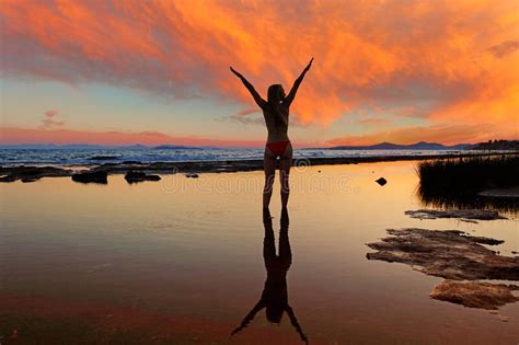 Silhouette Of Young Woman Standing On The Beach At The Sunset Stock