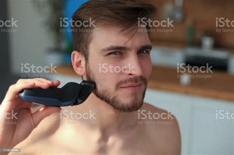 면도 절차 잘 생긴 젊은 남자는 거울 앞에 서있는 동안 전기 면도기로 얼굴을 면도 공란에 대한 스톡 사진 및 기타 이미지