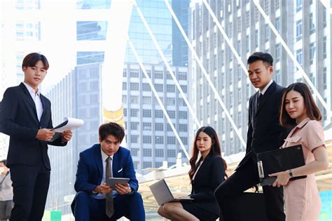 고층 빌딩이 흐릿한 배경으로 현대 도시 도심에서 사교하는 5 명의 젊은 아시아 기업 인그룹 사업가와 여성은 외부 사무실에서